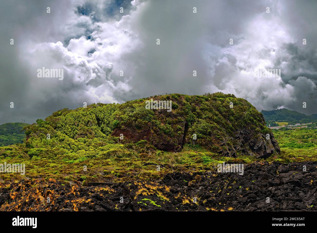 Green hills and dark volcanic rocks under a dramatic cloudy sky, lava ...