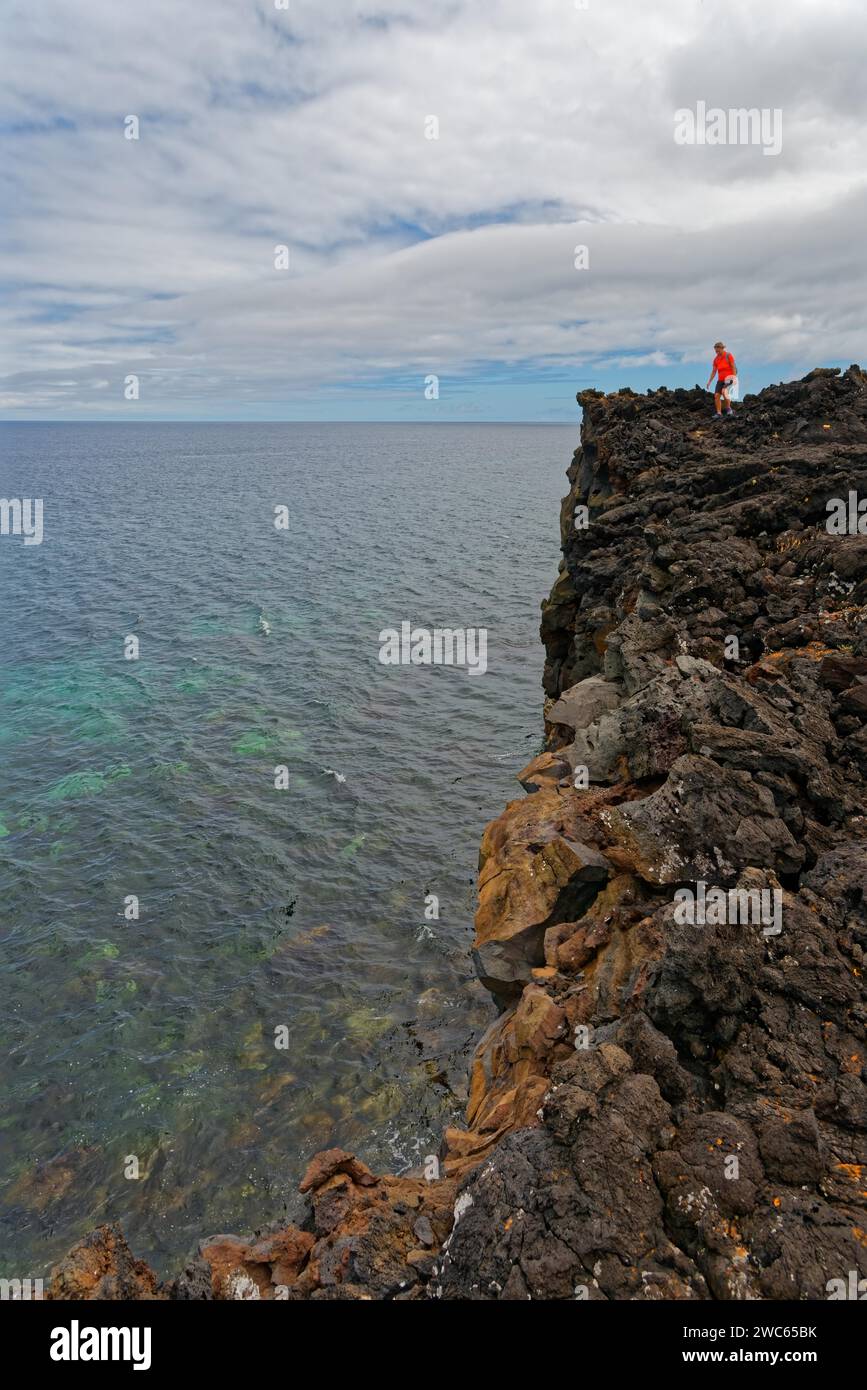 A brave person stands on the edge of a high volcanic cliff above the ...