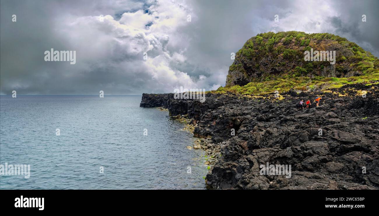 Group of people walking along a rocky coast with a cloudy sky above ...