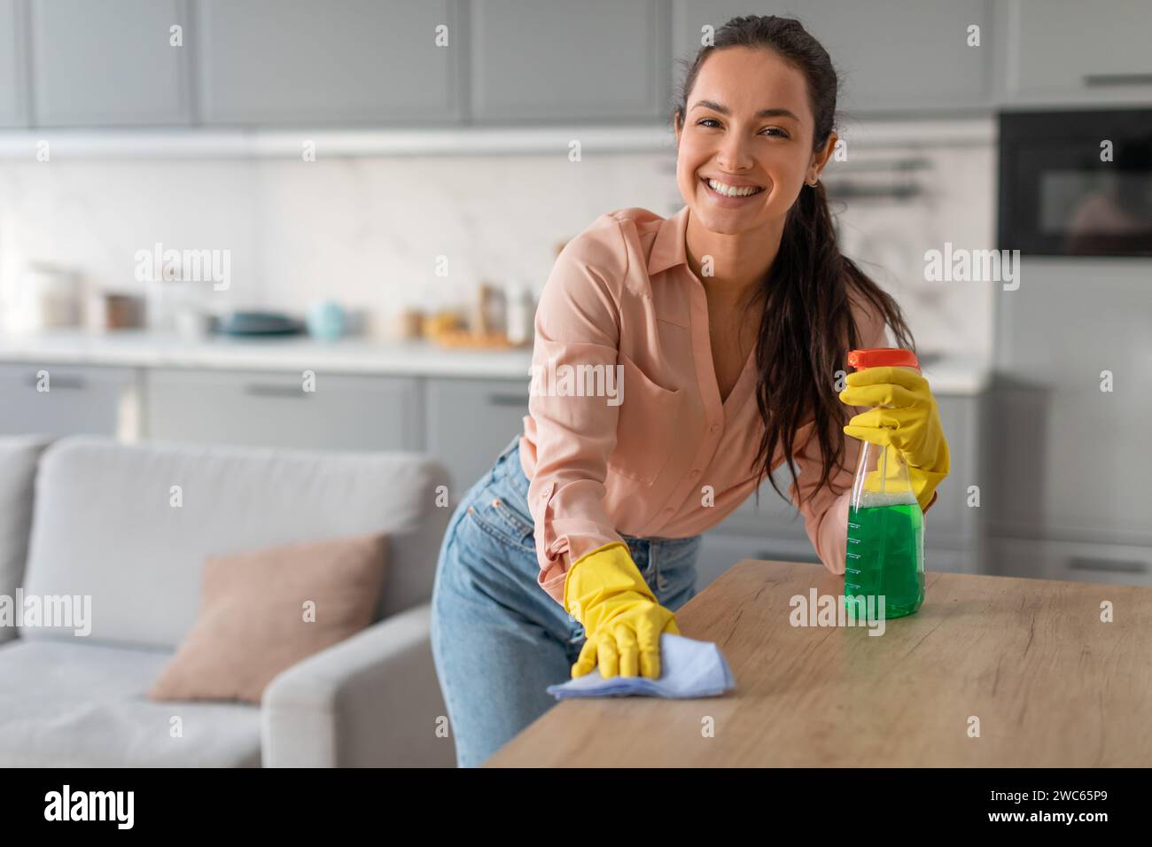 Smiling young woman wiping down table with cleaning spray and cloth Stock Photo - Alamy