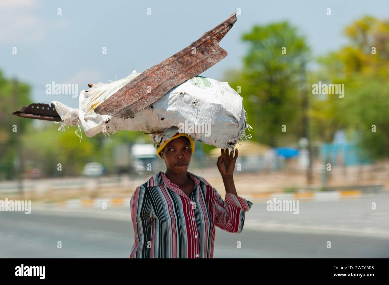 African woman carrying scrap metal on her head through the streets ...