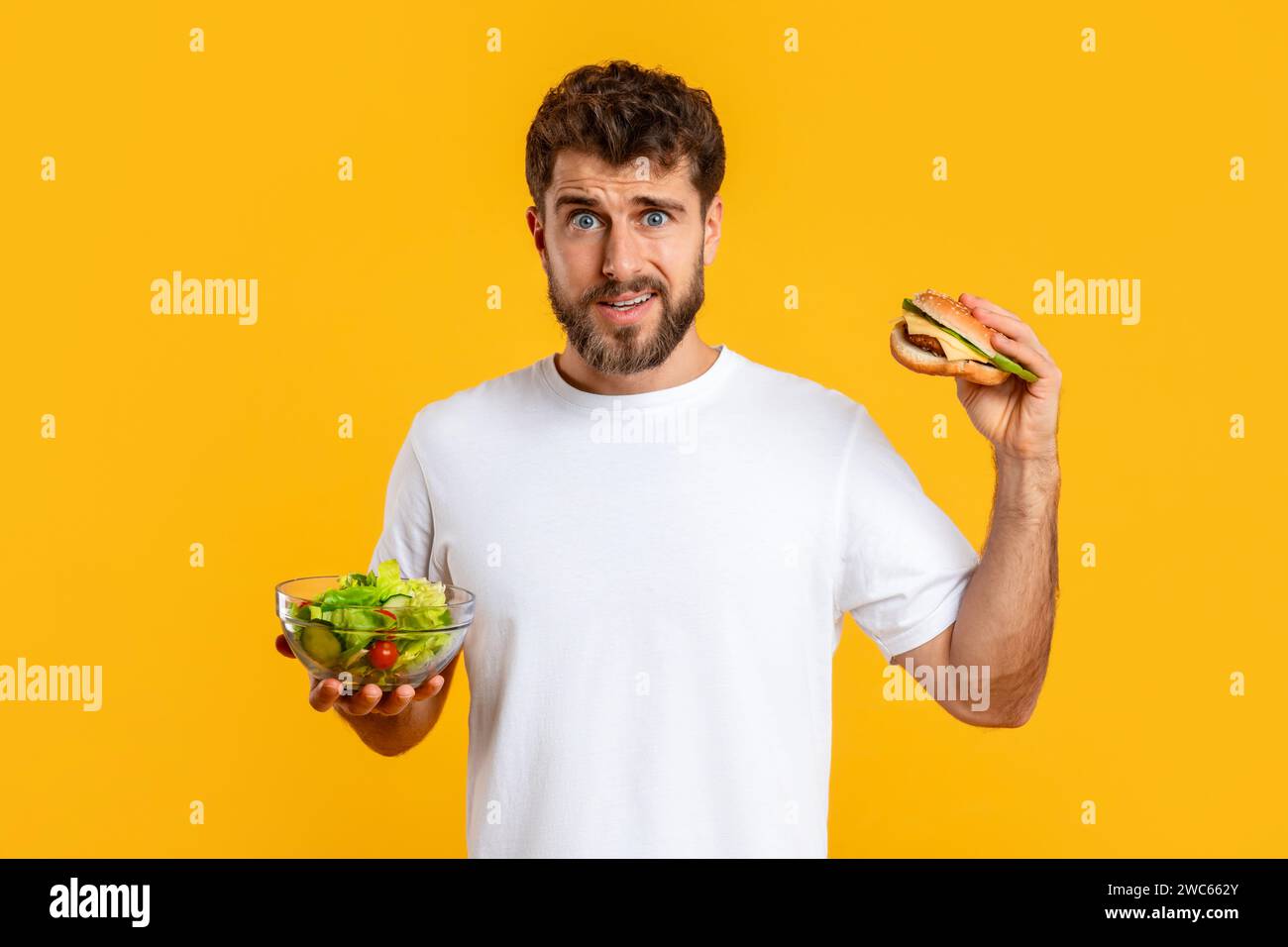 Confused Guy Holding Burger And Vegetable Salad Choosing Diet, Studio ...
