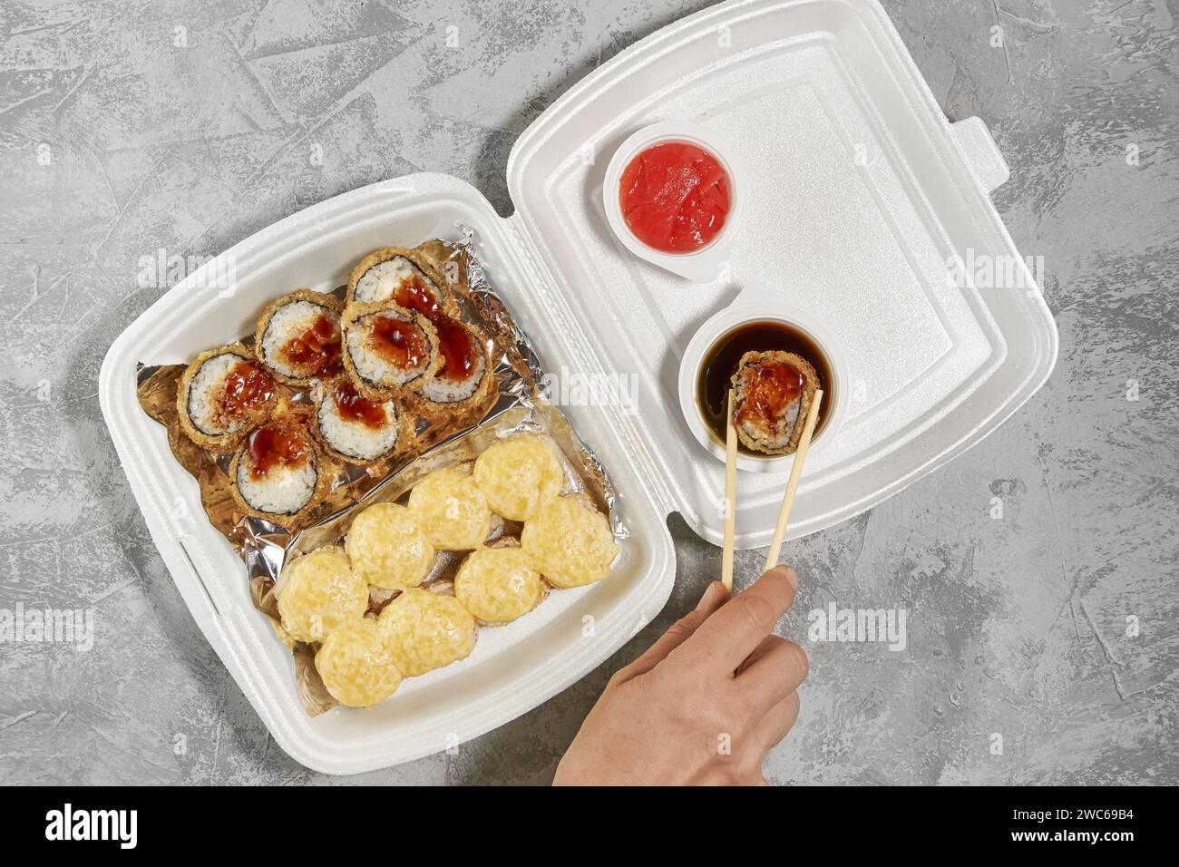 Delicious sushi rolls in disposable plastic boxes. The hand takes a ...
