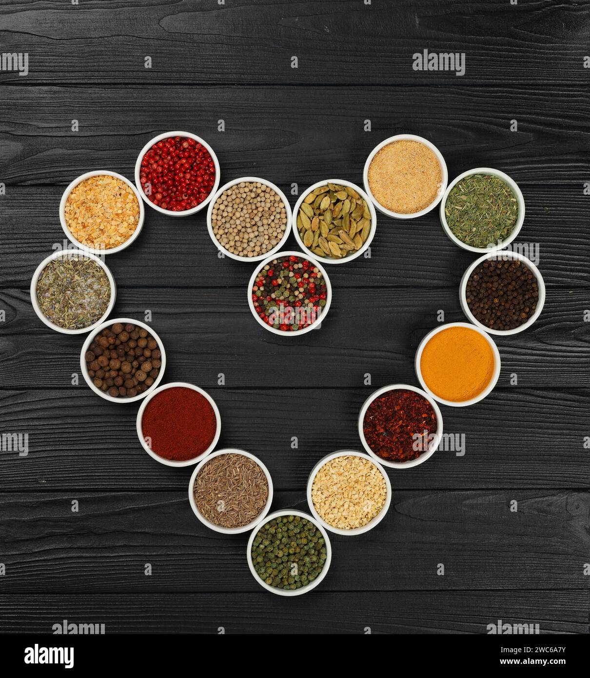 Heart shaped frame of assorted spices in white ceramic bowls over dark ...