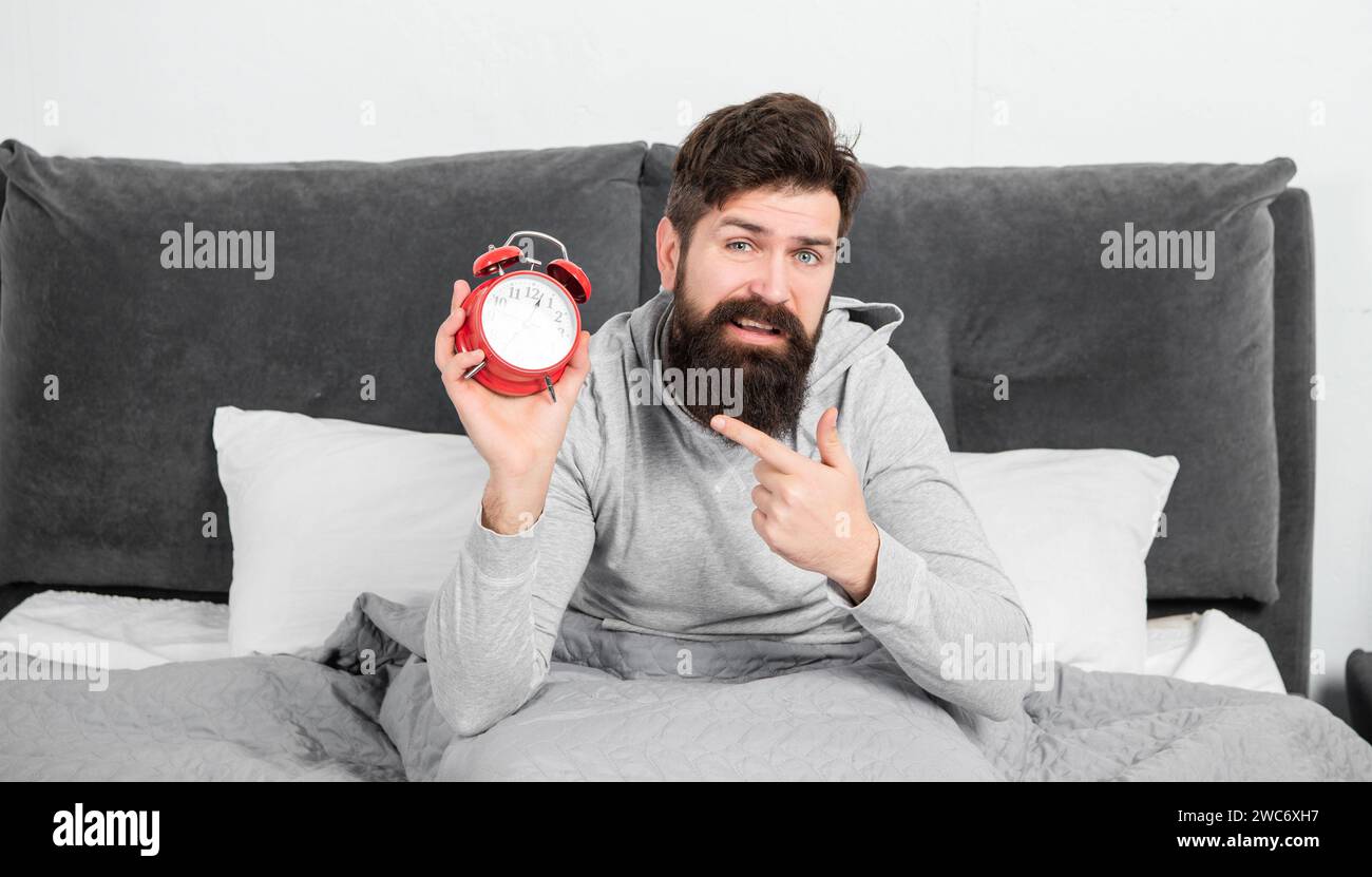 Sleepy man pointing finger at alarm clock being in bed awake, morning ...