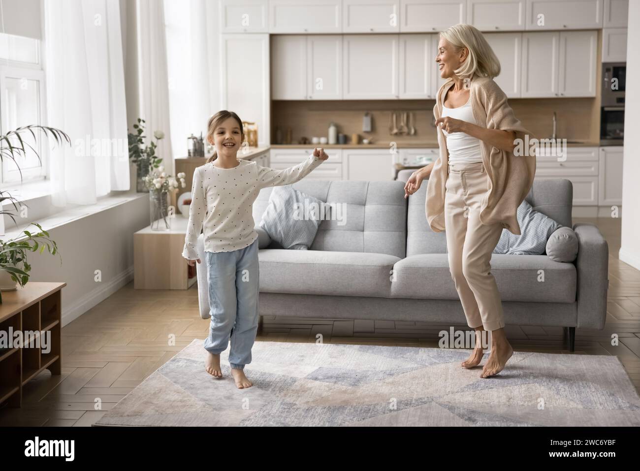Cheerful granddaughter child and happy active grandma dancing to music ...