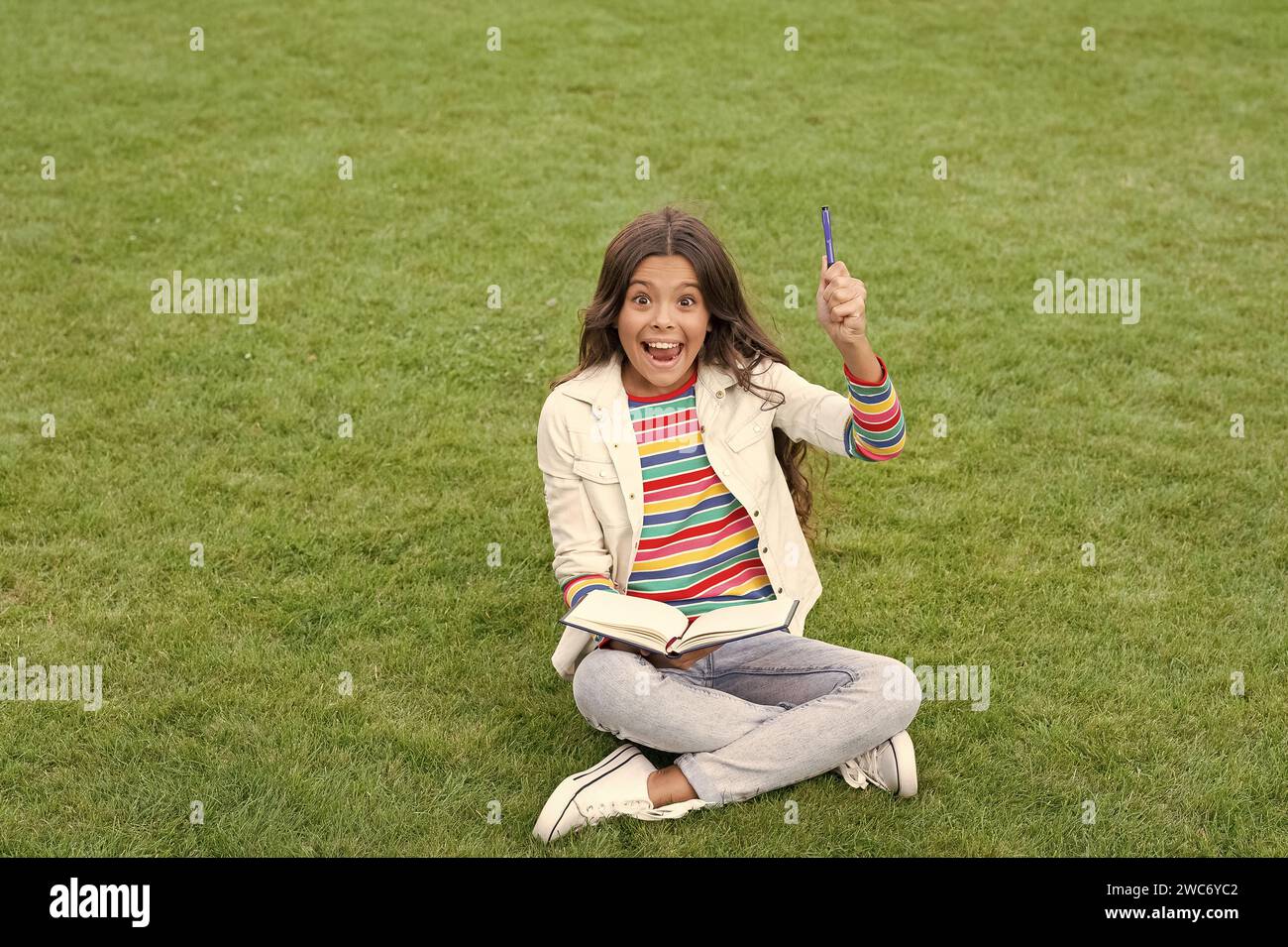 inspired teen girl making notes in notebook sitting on grass. taking ...