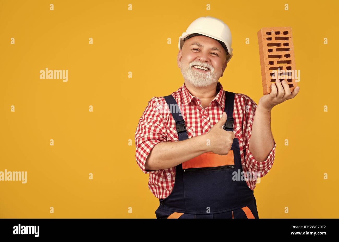 happy old aged man bricklayer in helmet on yellow background. thumb up ...