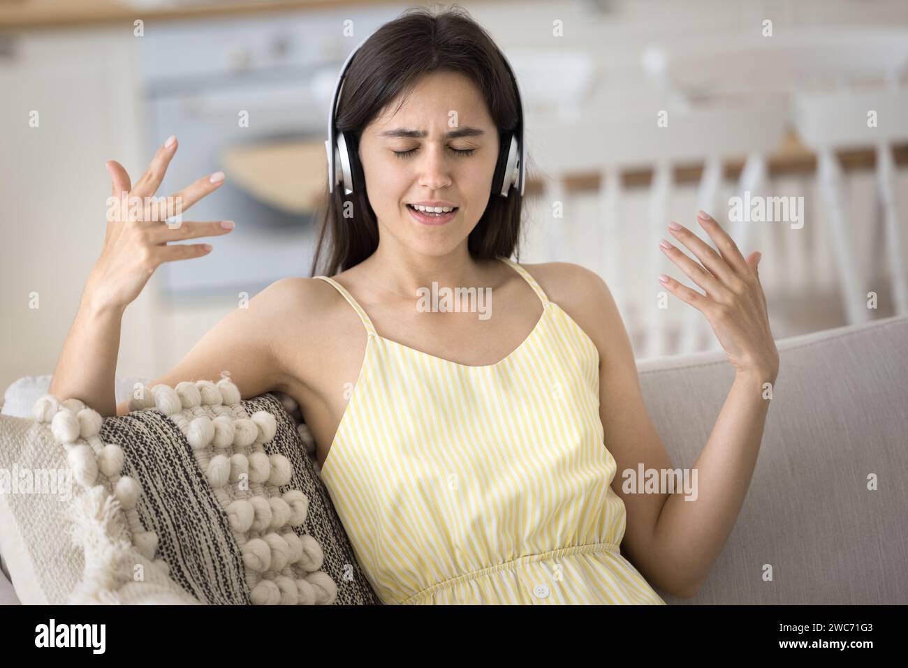 Woman in headphones sings a song seated on couch Stock Photo - Alamy