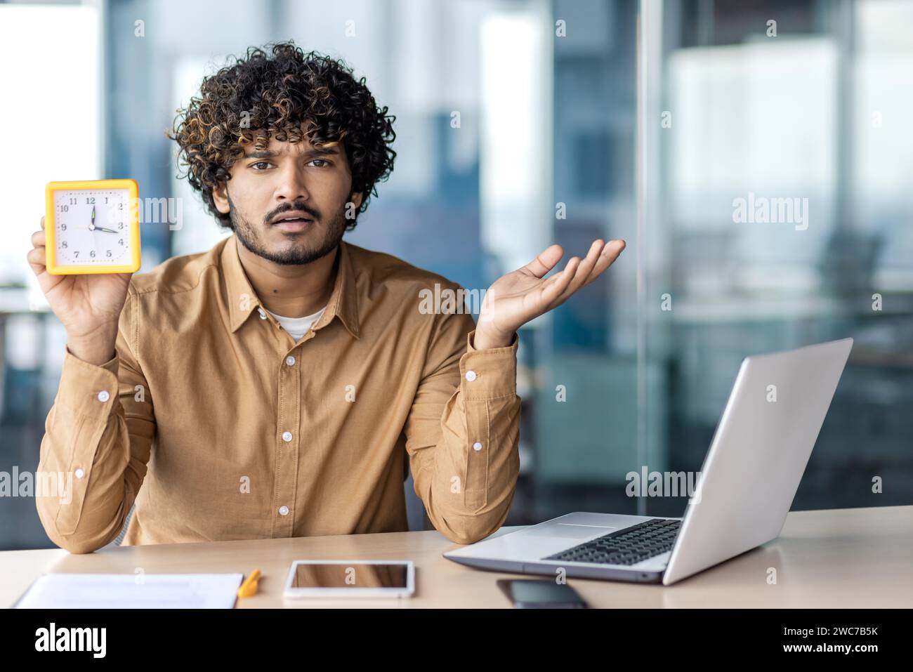 Bewildered male office worker holds an alarm clock, showing managing ...