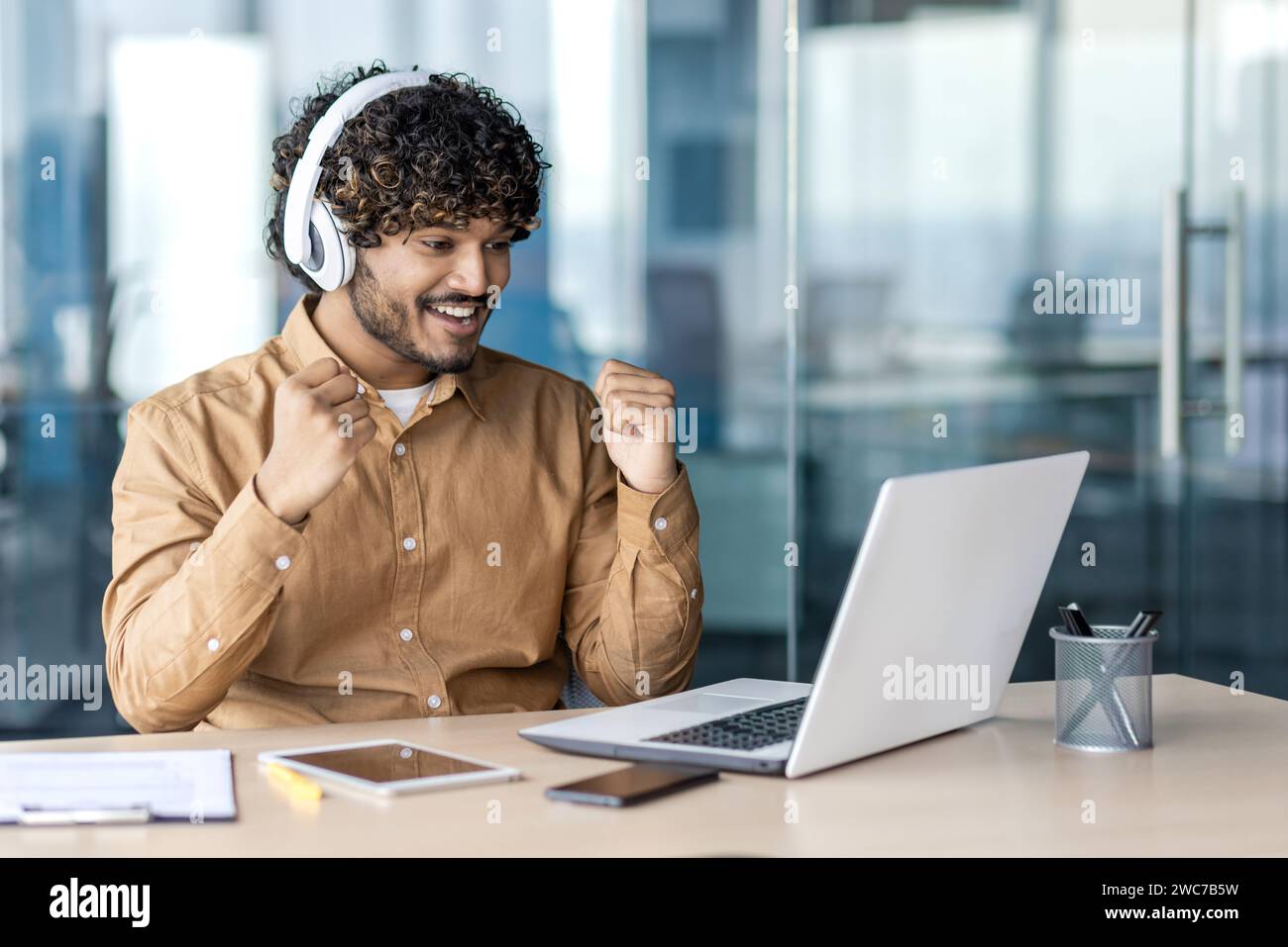 A cheerful young adult in casual wear with headphones enjoying music ...