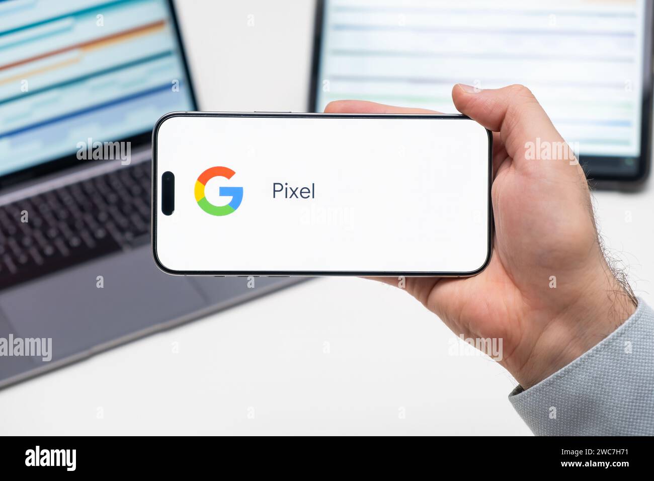 Google Pixel logo of app on the screen of mobile phone held by man in front of the laptop and ...