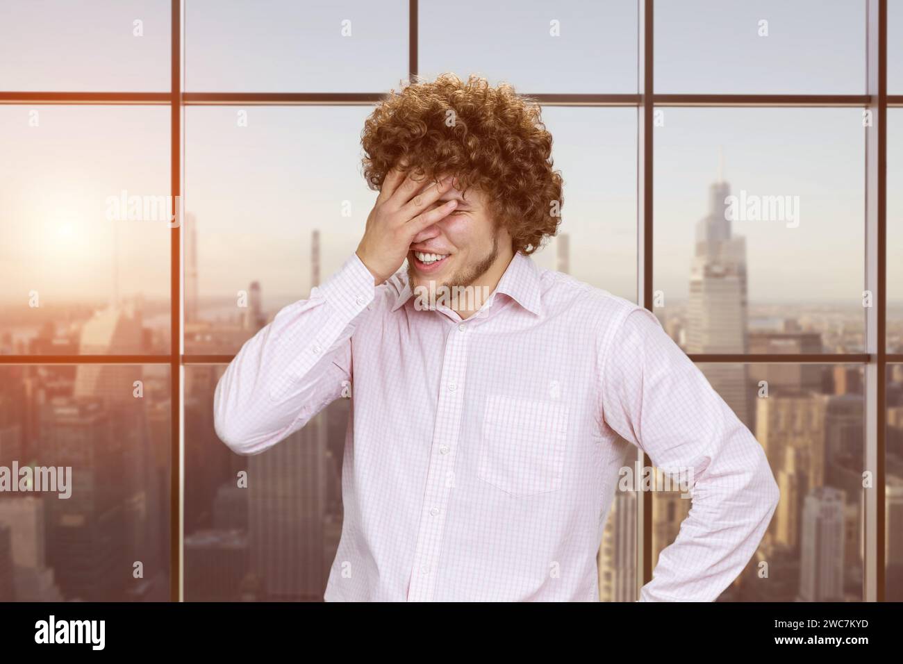 Portrait of a young man with curly hair facepalming because of a cringe ...