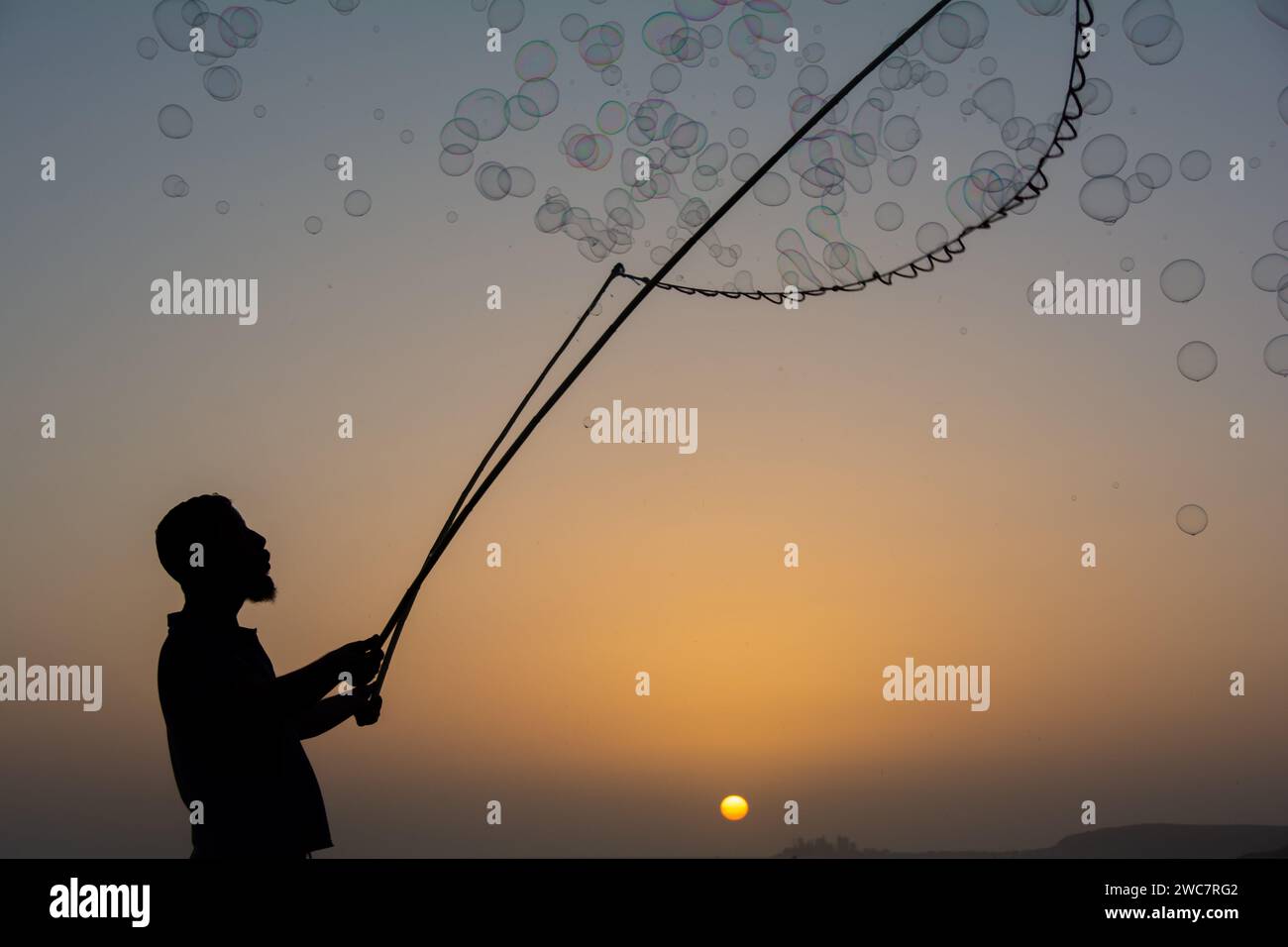 A man in silhouette makes lots of soap bubbles with a soap bubble stick ...