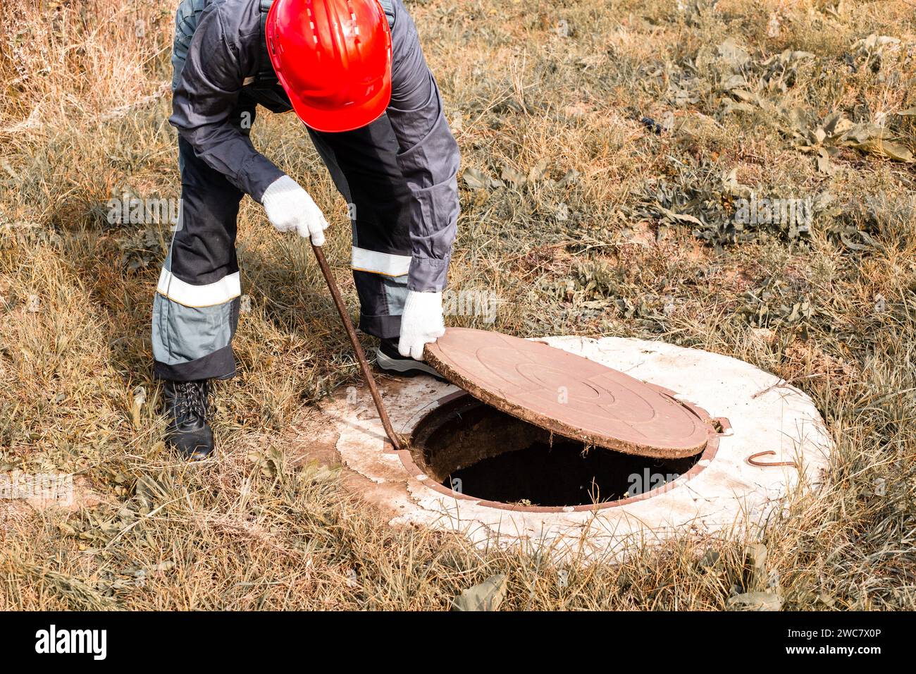 plumber in a helmet lifts the manhole cover of a water well. Inspection ...
