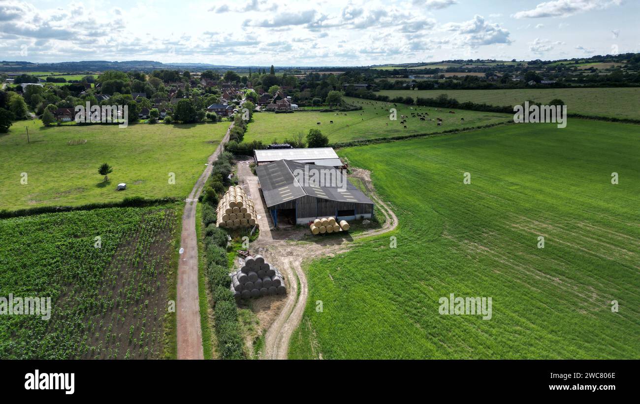 A drone image of a farm building with hay bails to one side. Green ...
