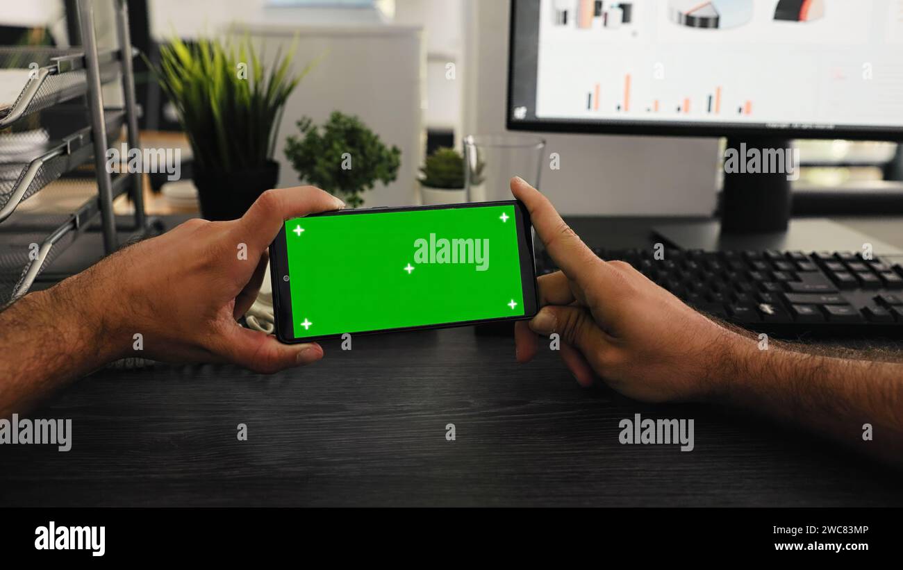POV of worker holds phone with greenscreen display at desk, working ...