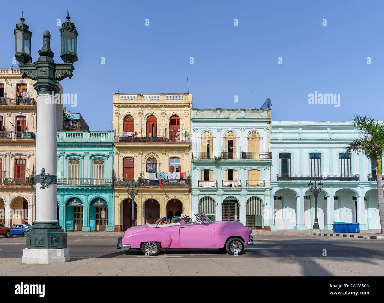 a pink american convertible driving past colorful buildings in old ...