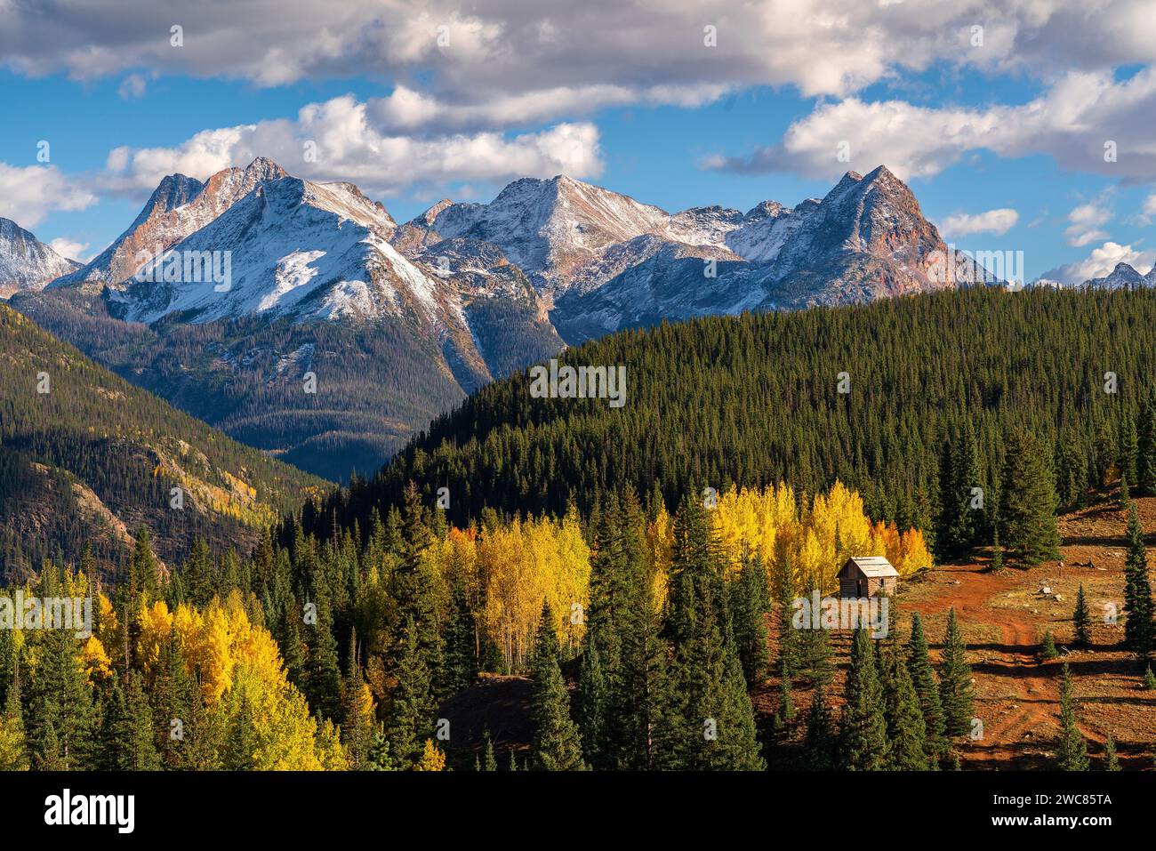 Mining shack nestled in aspens and pine forest beneath snow-covered ...