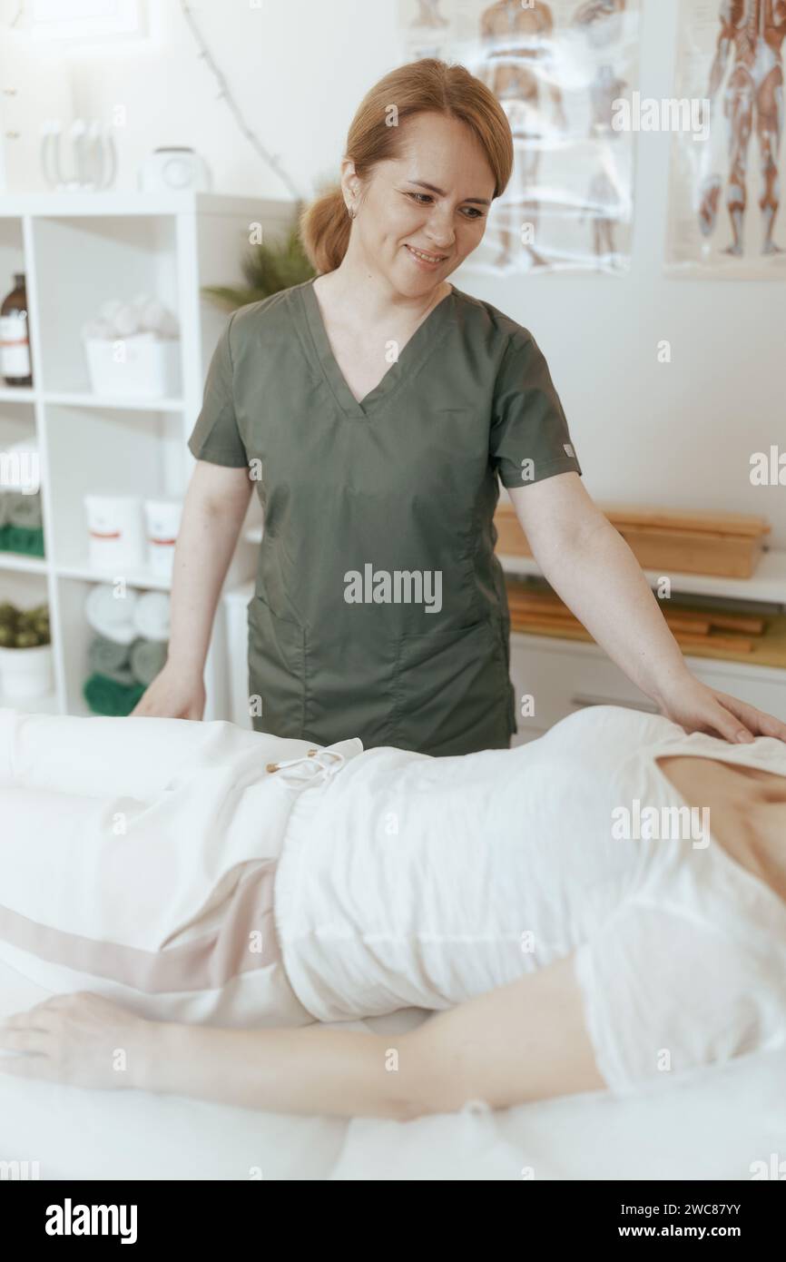 Healthcare time. happy female massage therapist in massage cabinet with client conducting ...