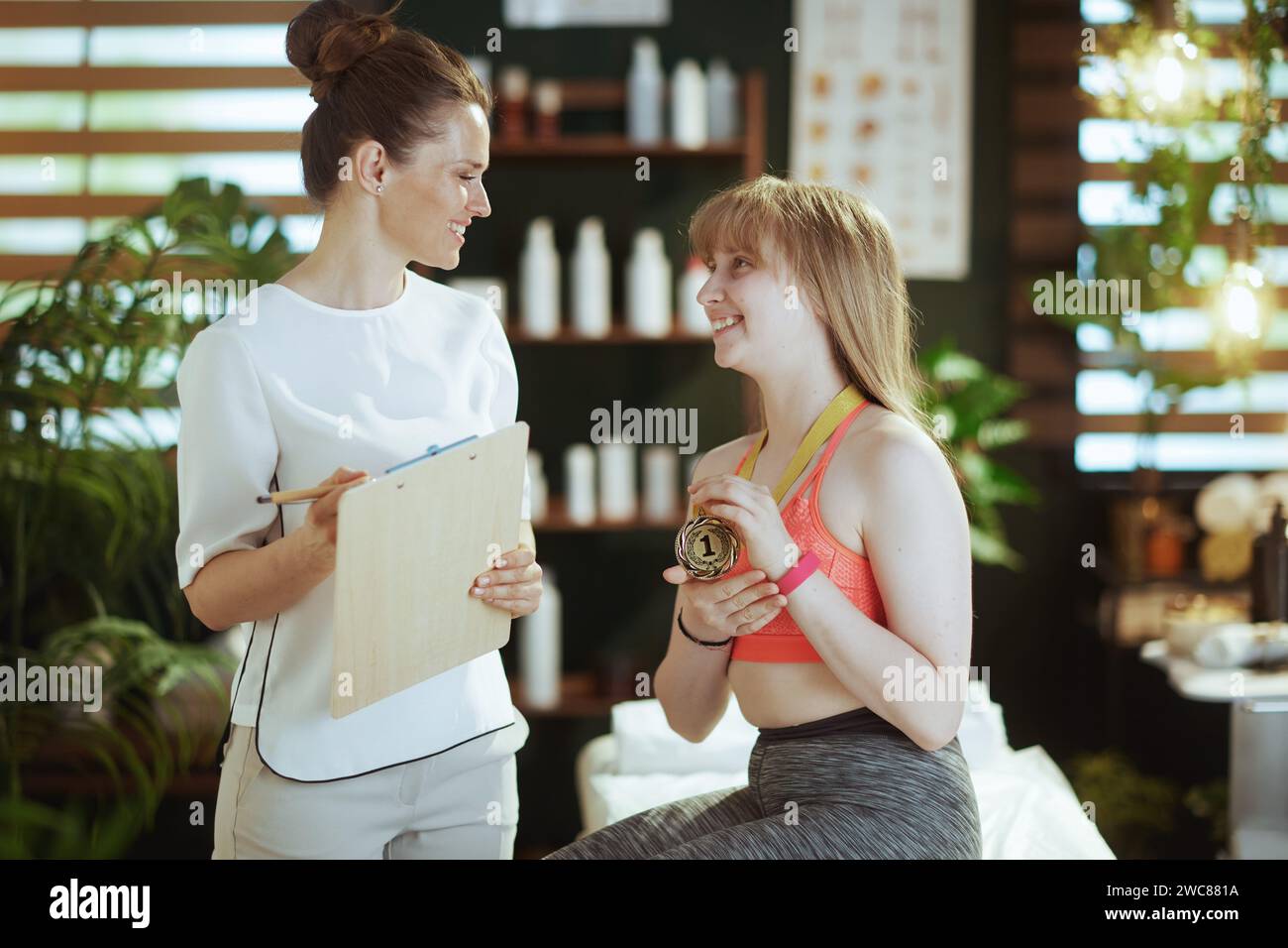 Healthcare time. smiling female massage therapist in massage cabinet with clipboard, teenage ...