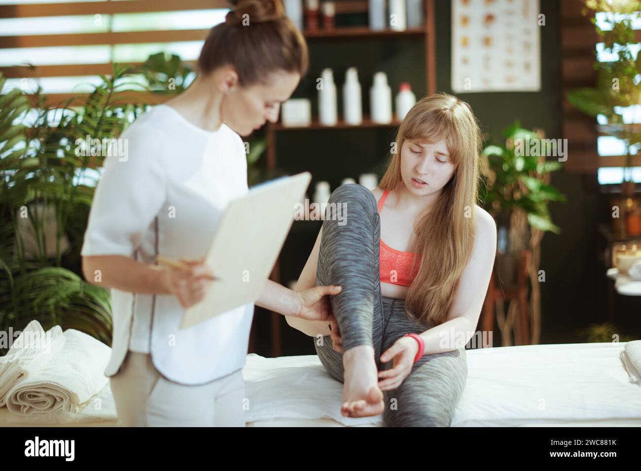 Healthcare time. concerned massage therapist woman in massage cabinet with clipboard and teenage ...
