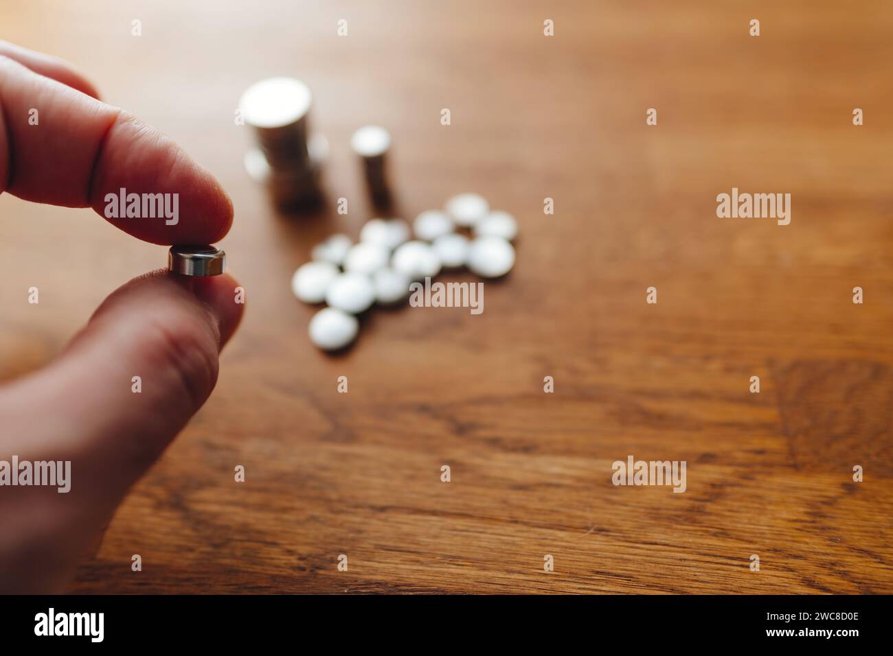 A person carefully picks up a small button battery from a wooden ...
