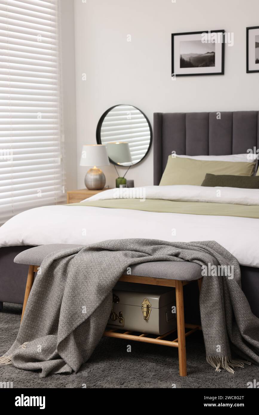 Horizontal blinds on window, comfortable bed and ottoman with blanket ...