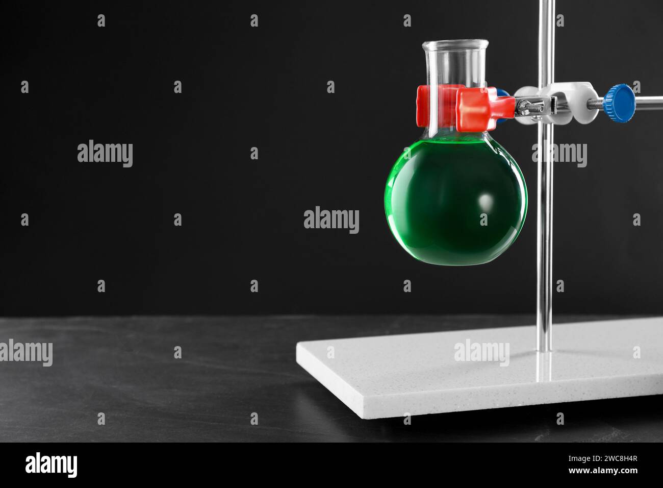 Retort stand and laboratory flask with liquid on table against black ...