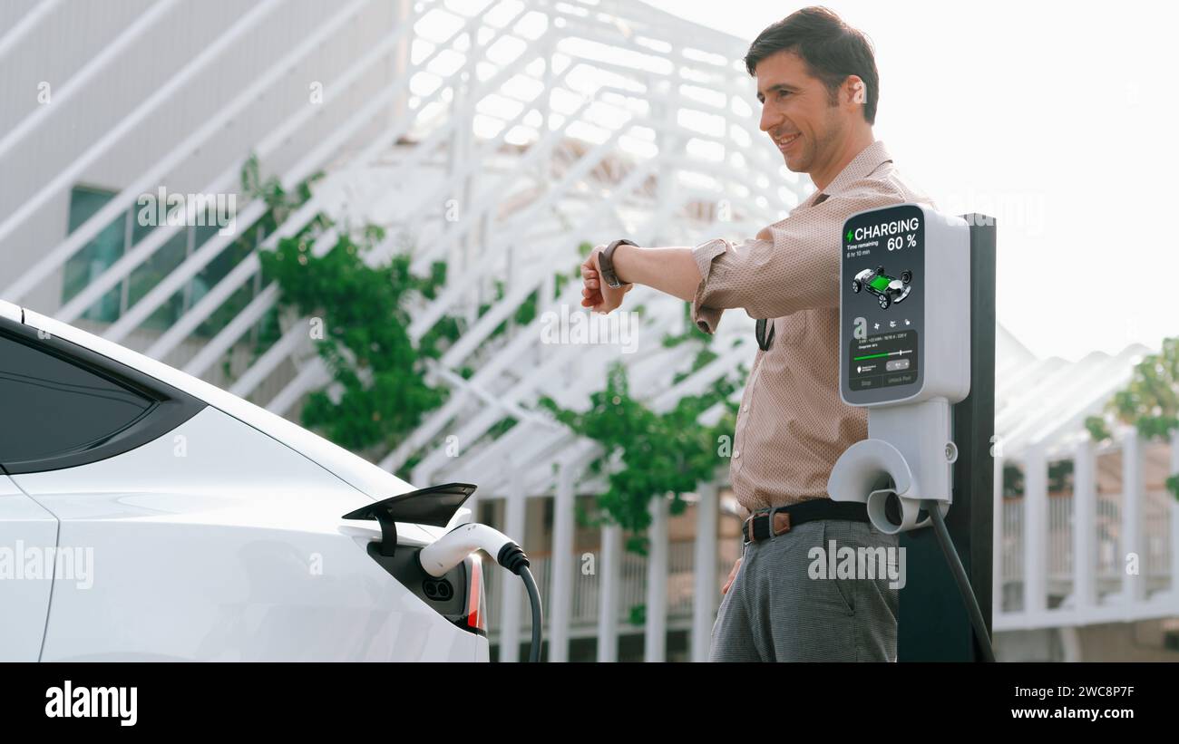 Young man checking time on smartwatch while EV charger to recharging ...