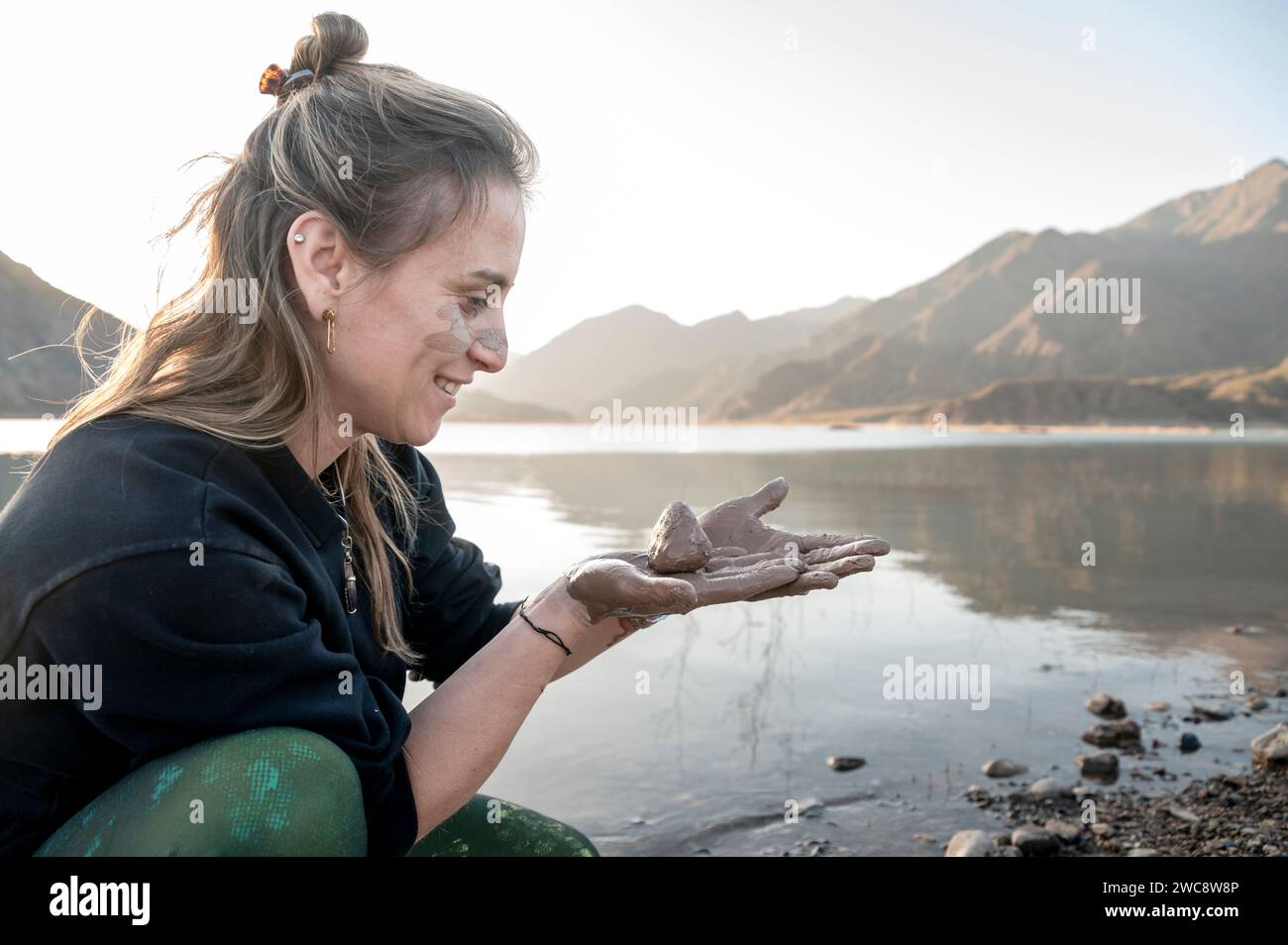 Woman putting mud on hands and face while enjoying outdoors in nature ...