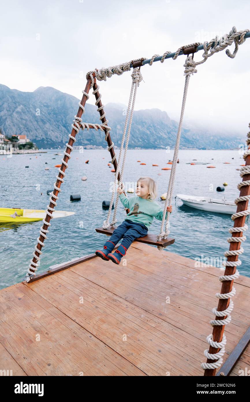 Little girl swings on a rope swing on a pier over the sea Stock Photo ...