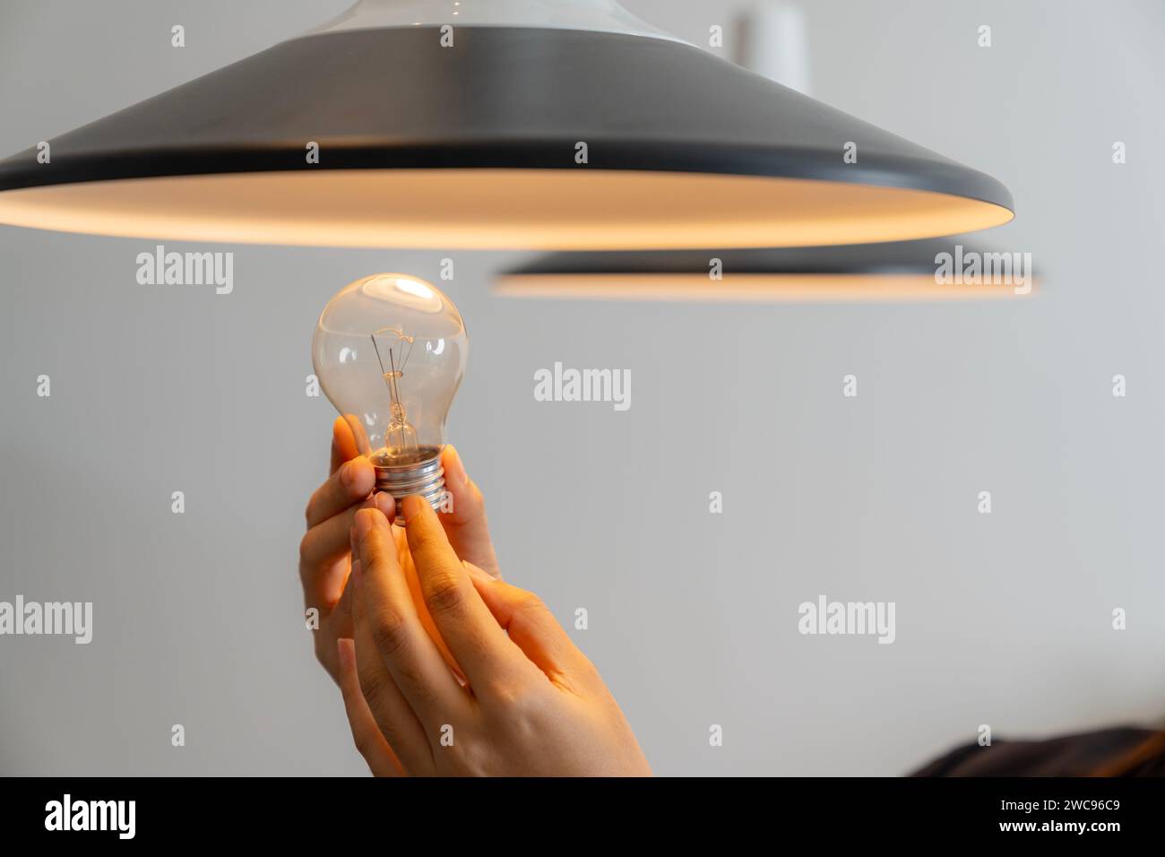 A young woman is changing a light bulb from an incandescent bulb to an ...
