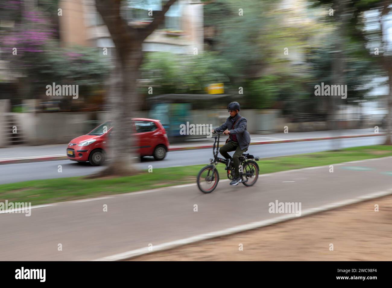 A cyclist on a bike path in the city, racing with a passing car. Image ...