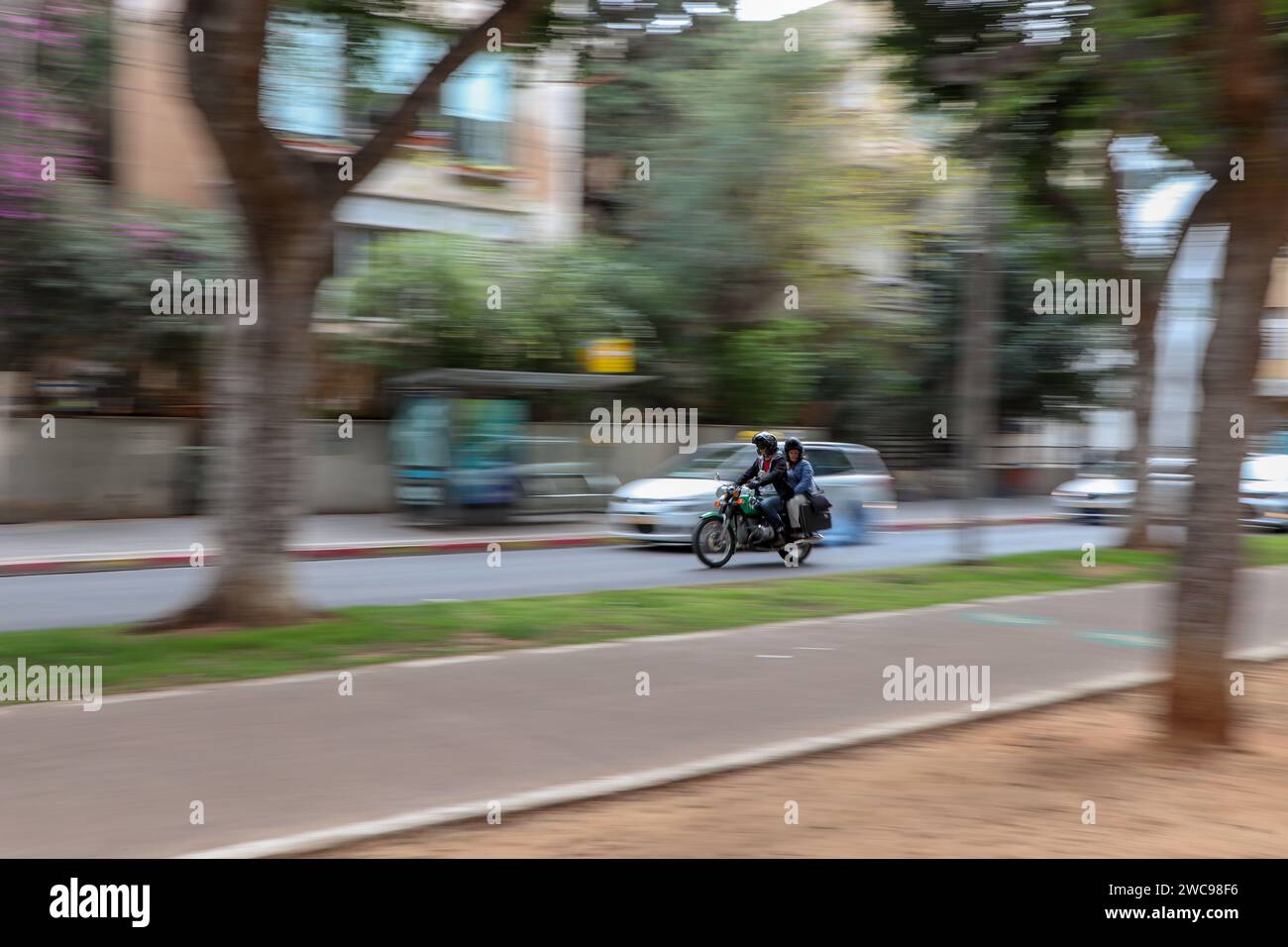 A couple rides a motorcycle between cars. Image in motion on a blurred ...