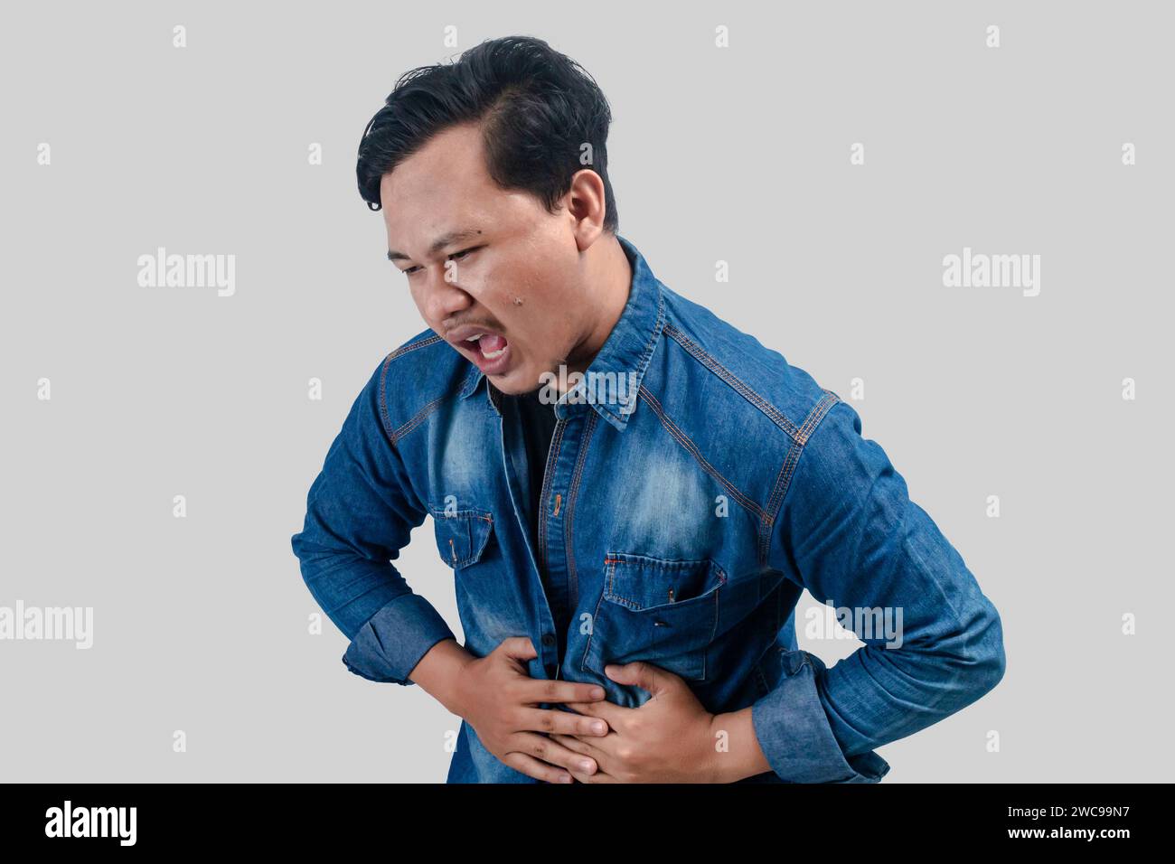 Young asian man having stomach ache or indigestion and pressing his stomach on isolated white ...