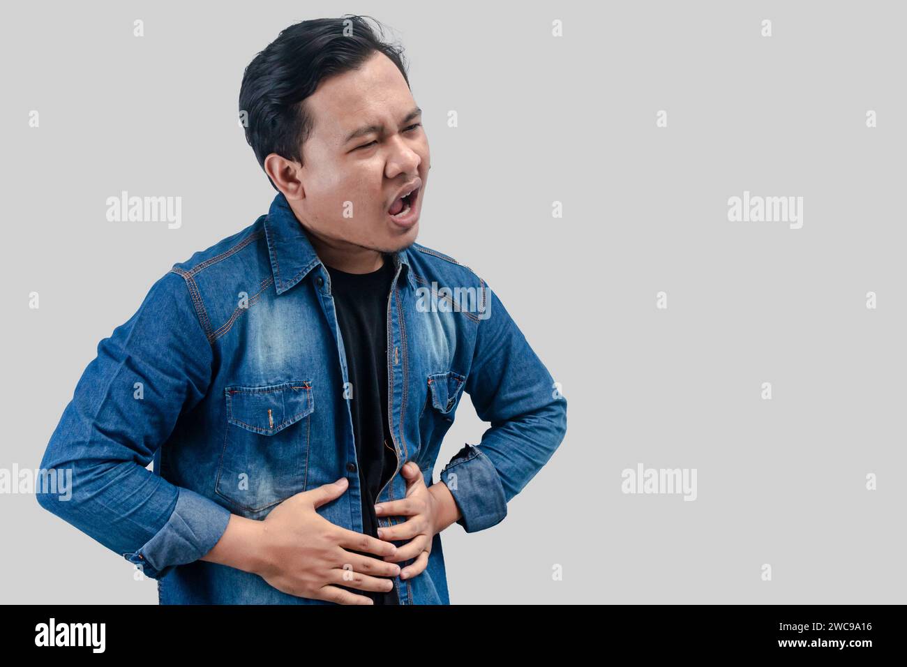 Young asian man having stomach ache or indigestion and pressing his stomach on isolated white ...