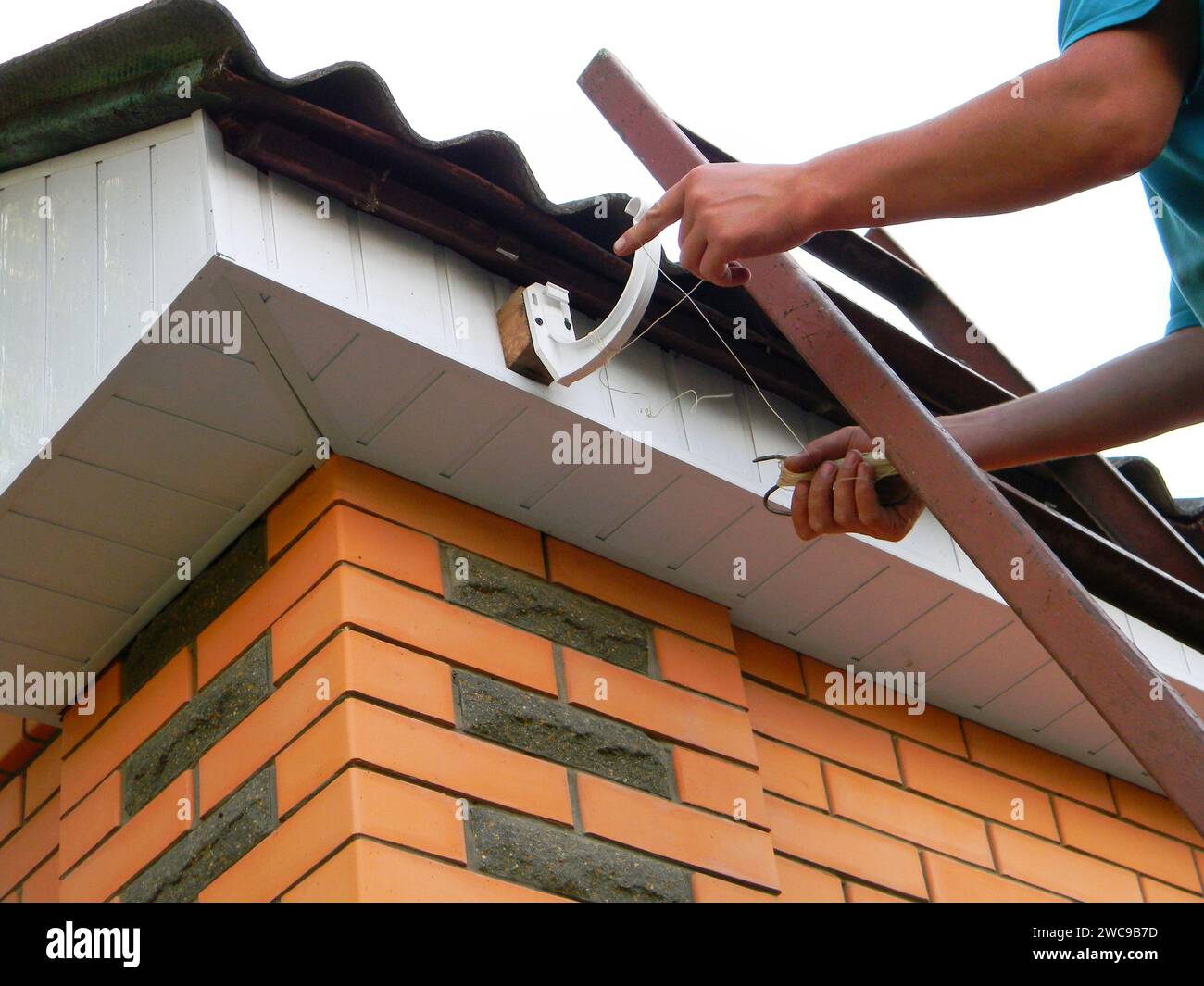 A building contractor is installing rain gutter system, fitting ...