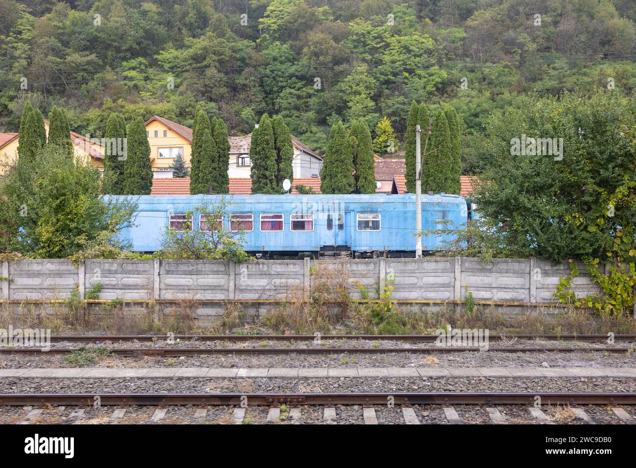 A blue train parked in a residential area, along a set of railroad ...