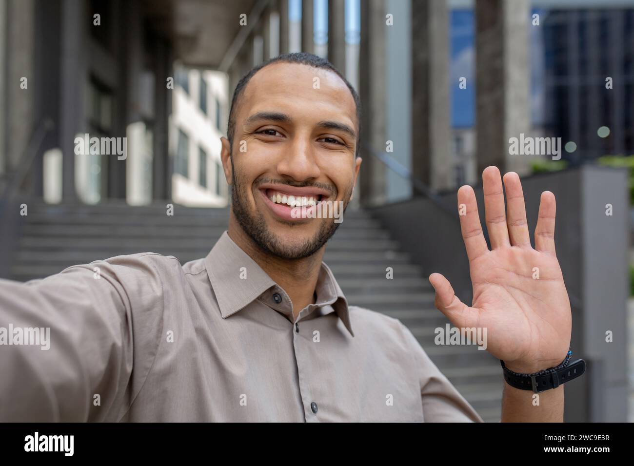 Cheerful young man taking a selfie, waving hand in greeting with a ...
