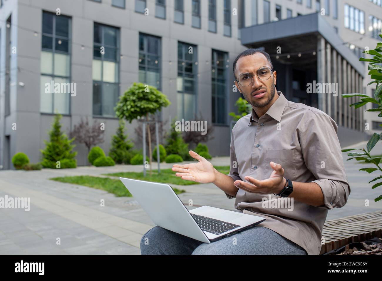 Confused businessman with laptop outdoors, expressing uncertainty ...