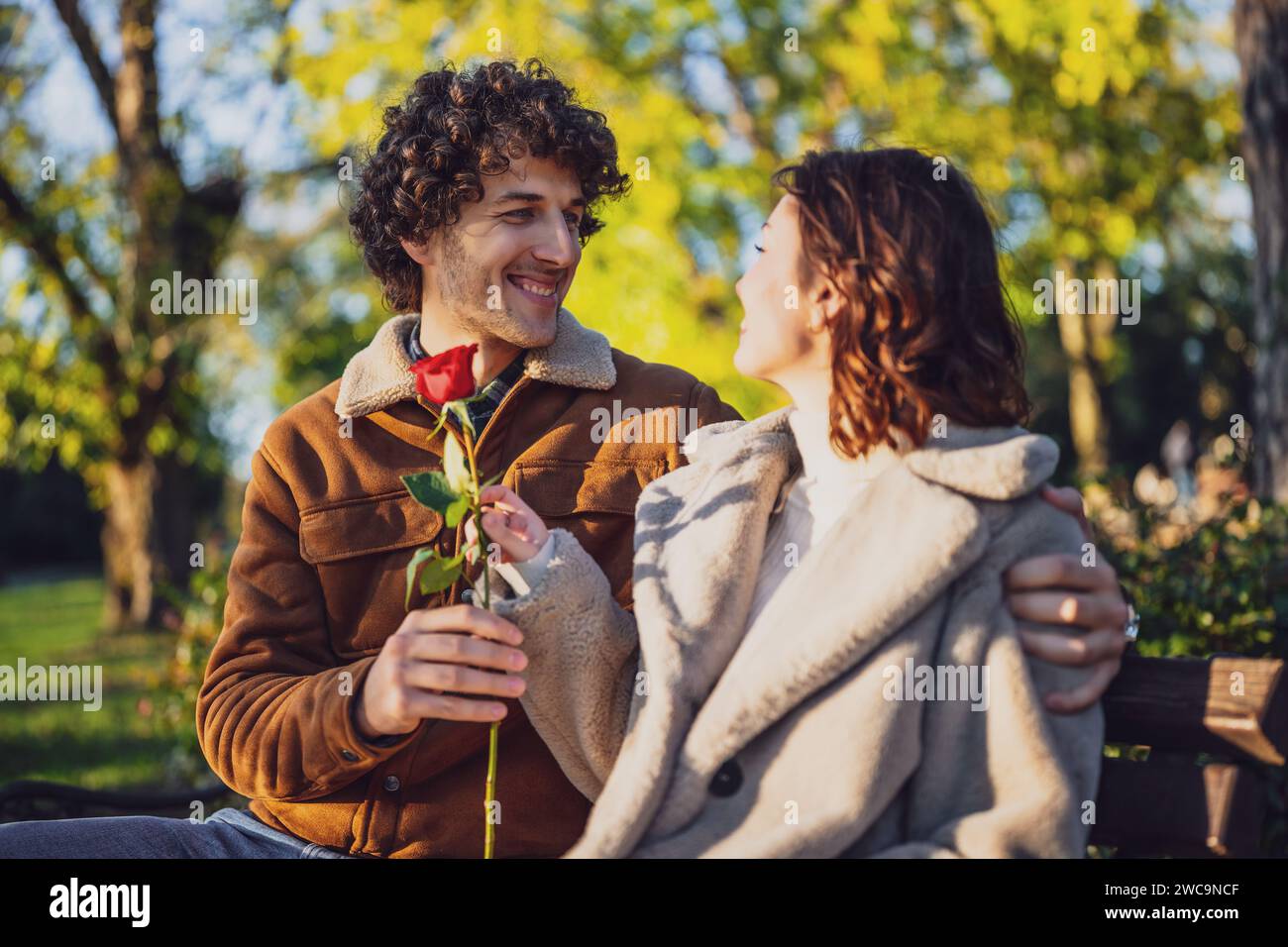 Portrait of happy loving couple in park. Man is giving rose to his ...