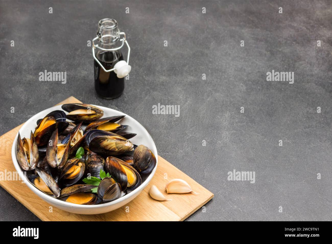 Mussels with open shells in white bowl on cutting board. Bottled water ...