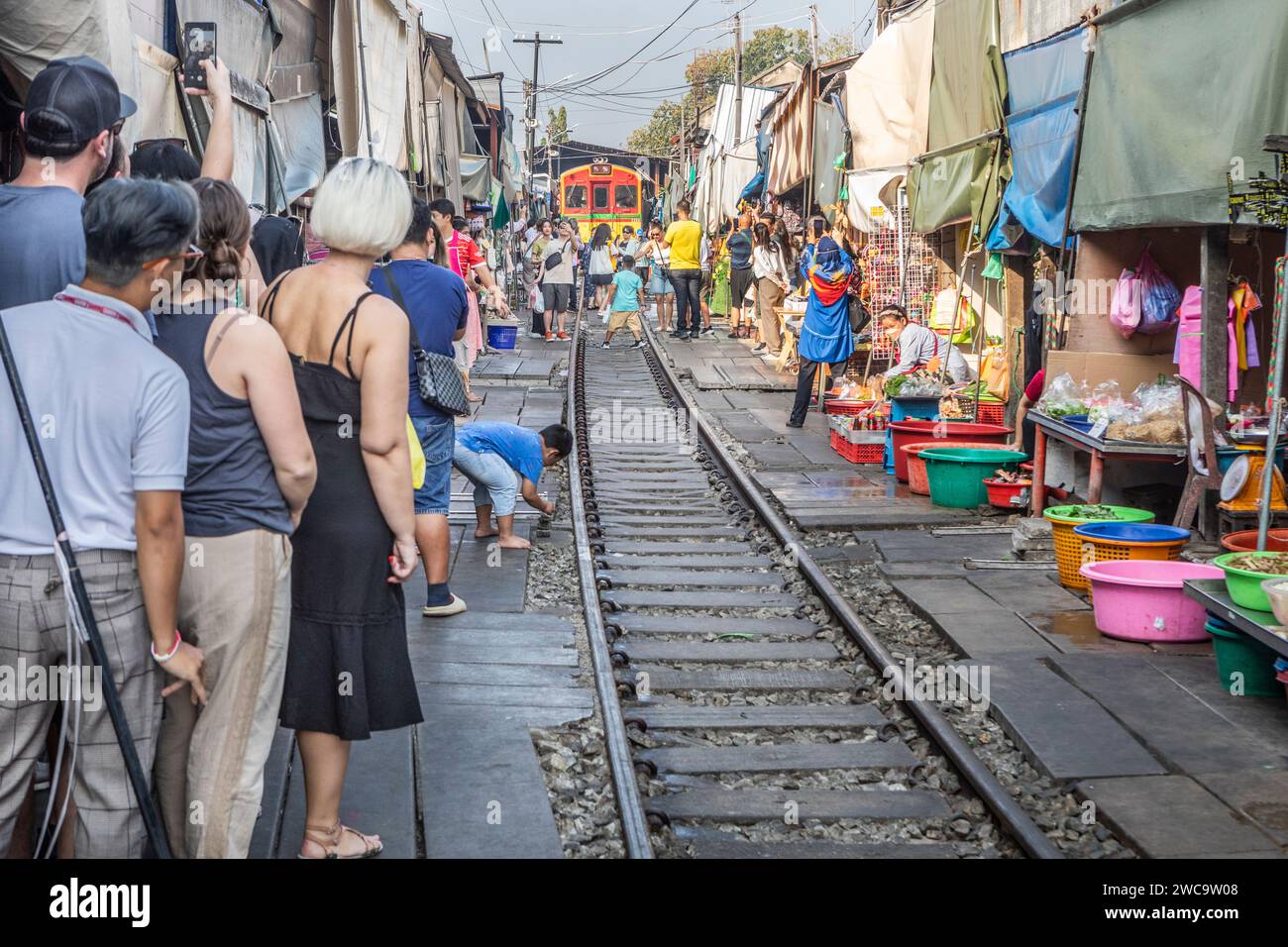 Tourists watching a train run slowly through Mae Klong Railway Market ...