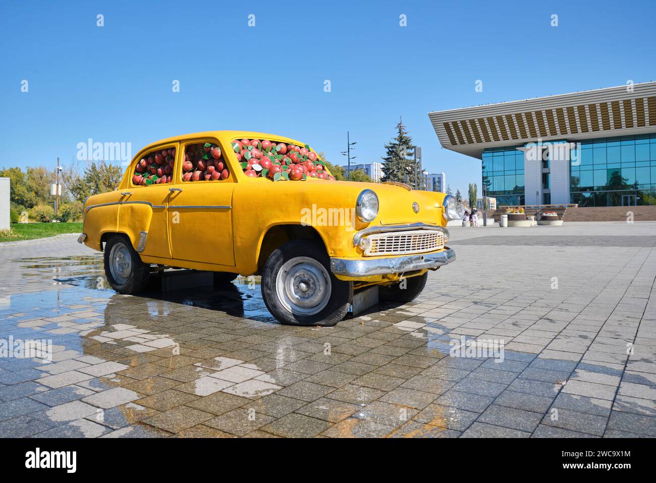 An old yellow Moskvich car, filled with fake red apples. It is an art ...