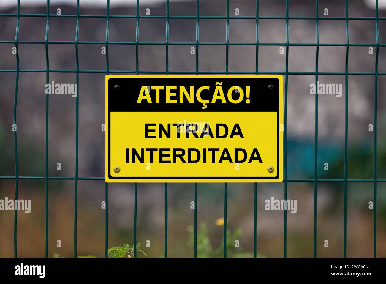 Yellow warning sign on a fence stating in portuguese: "Atenção ...