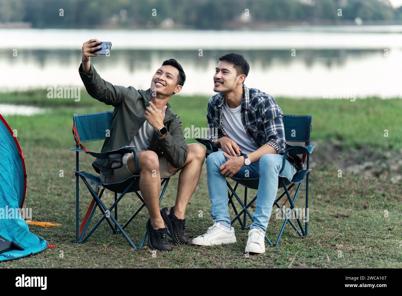 Gay LGBTQIA couple sitting on picnic chair taking selfie together while ...