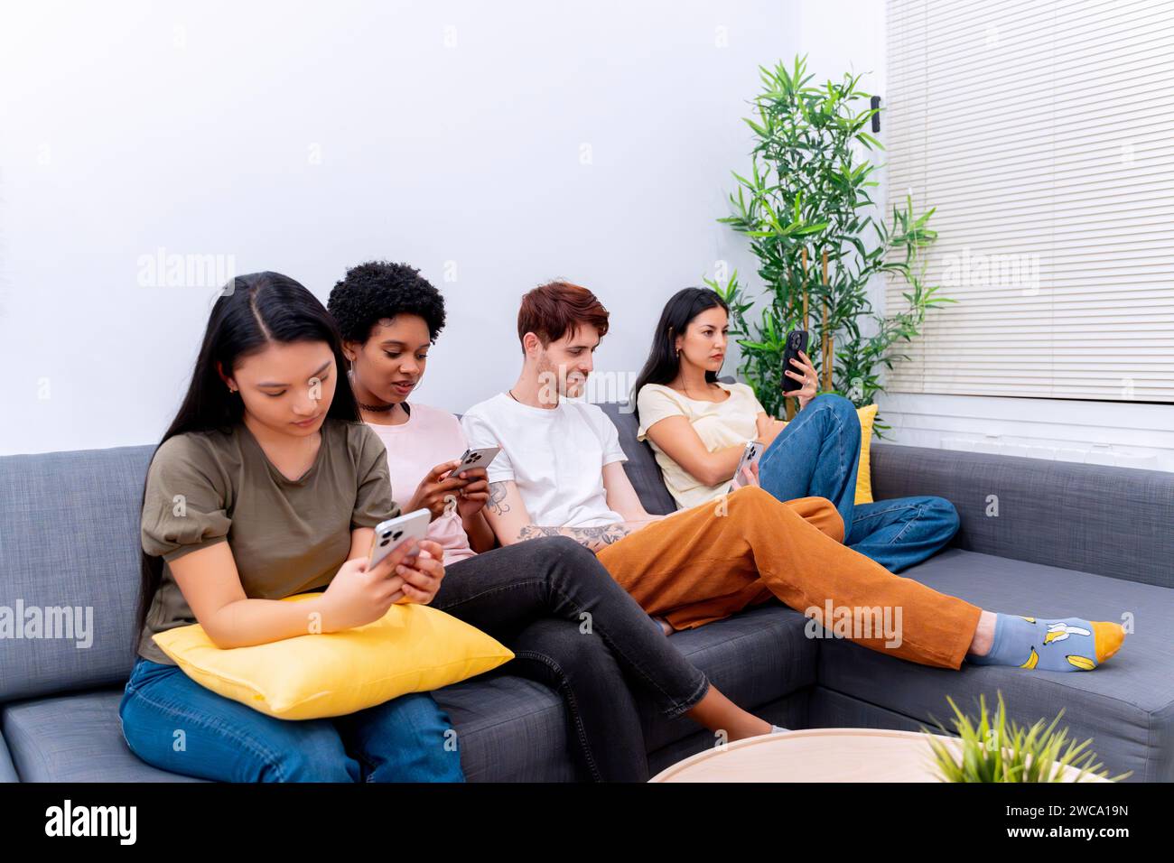 Group of young adults using smartphones on a couch in a home setting ...