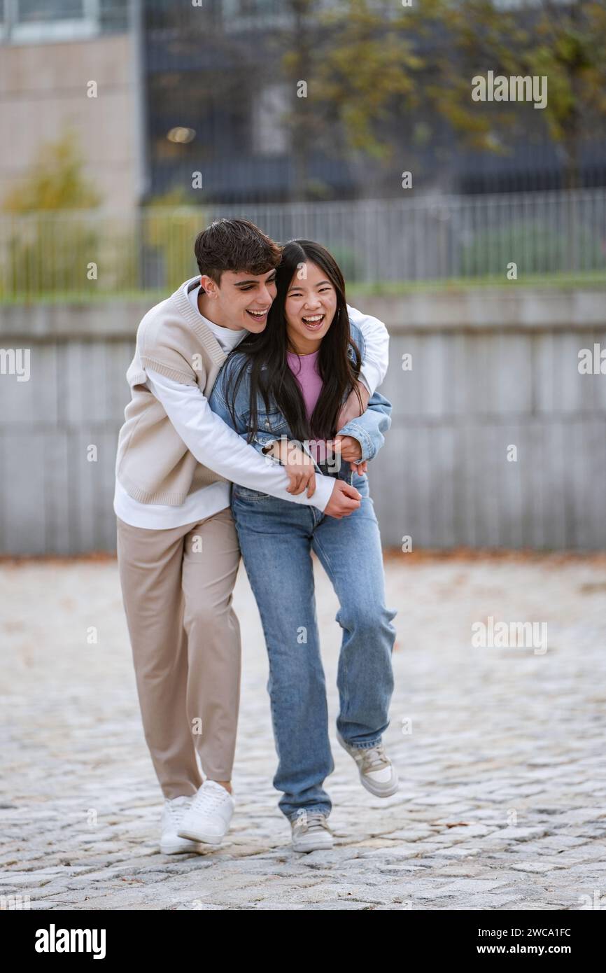 A young couple laughing and hugging while walking along a cobblestone ...
