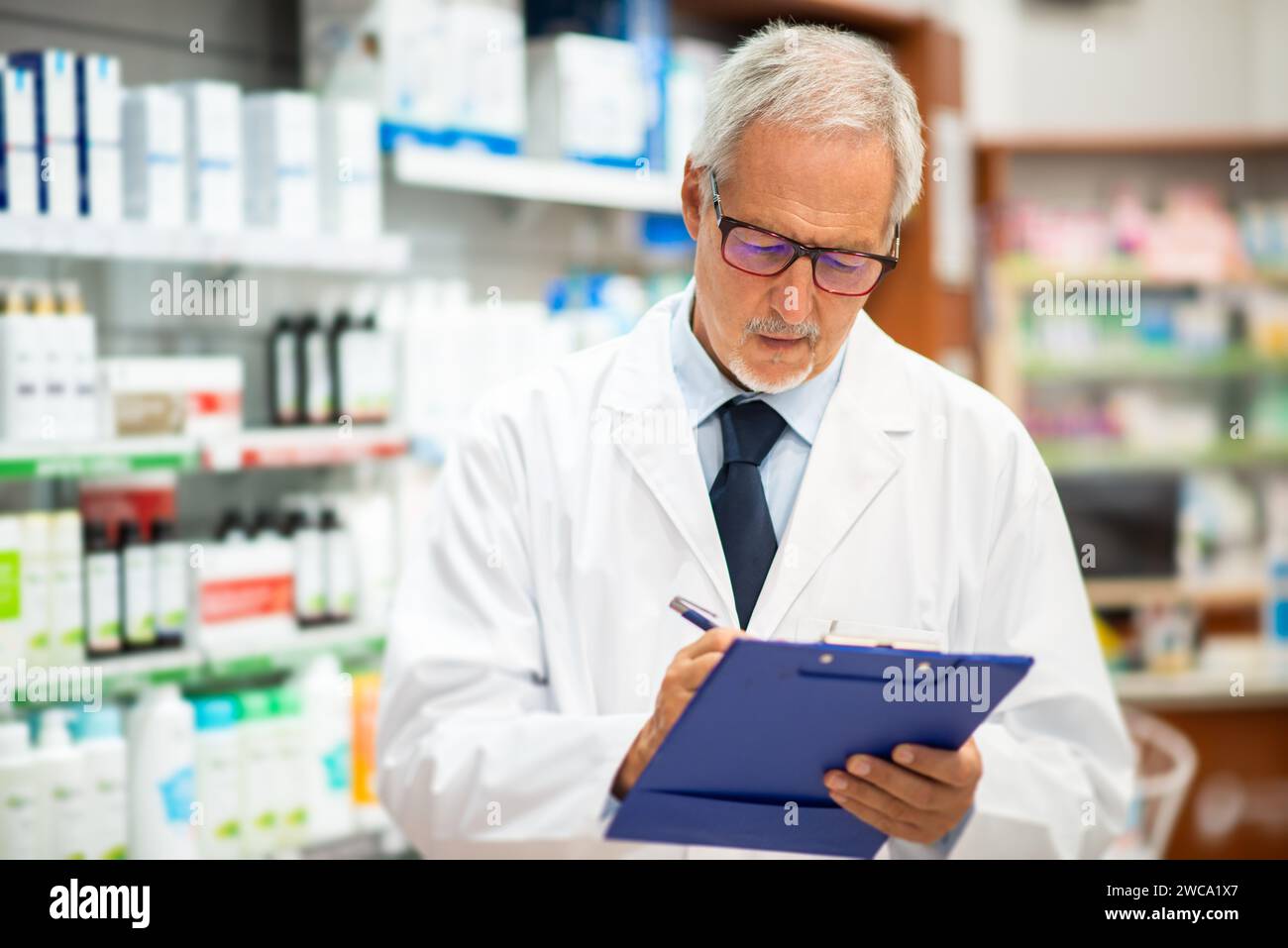 Senior pharmacist writing on a document while standing in his pharmacy ...